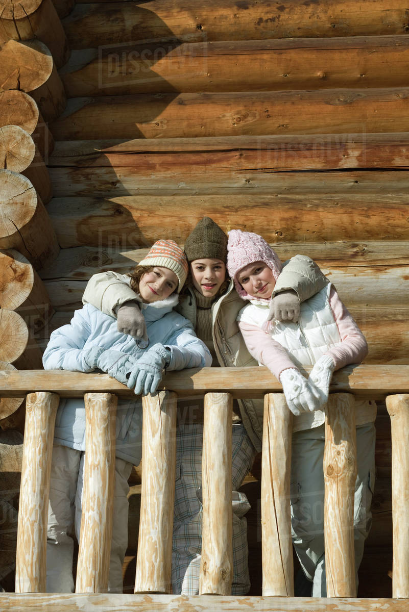 Three preteen or teen girls standing on deck of log cabin, smiling at ...