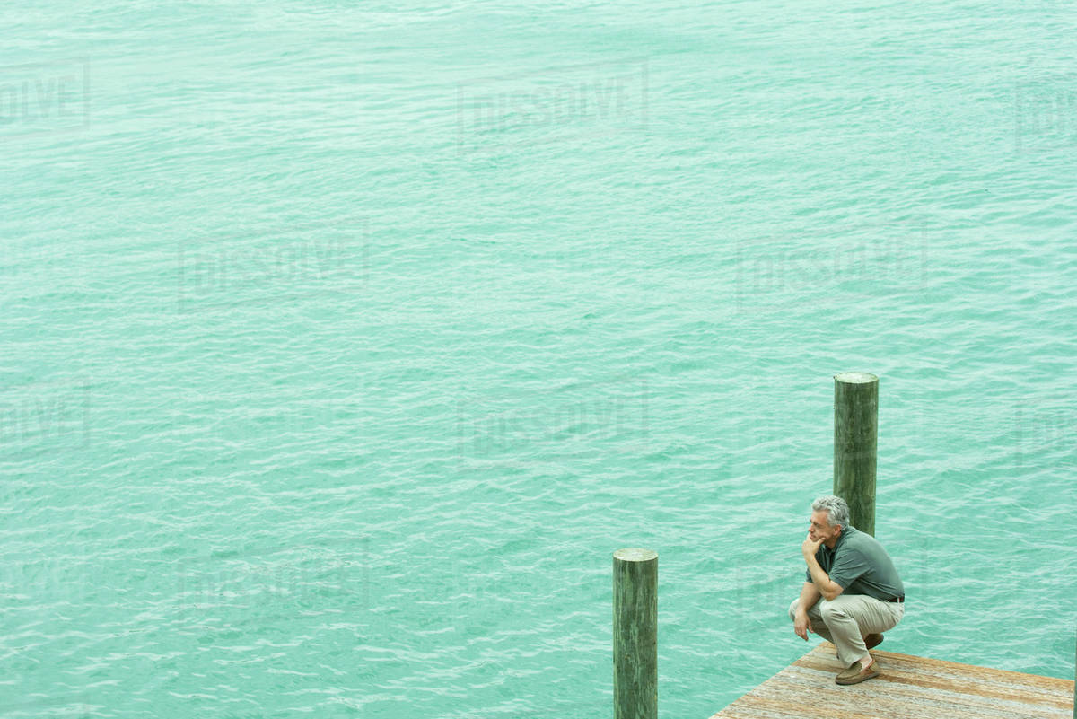 Man crouching on dock, holding head, high angle view - Royalty-free ...
