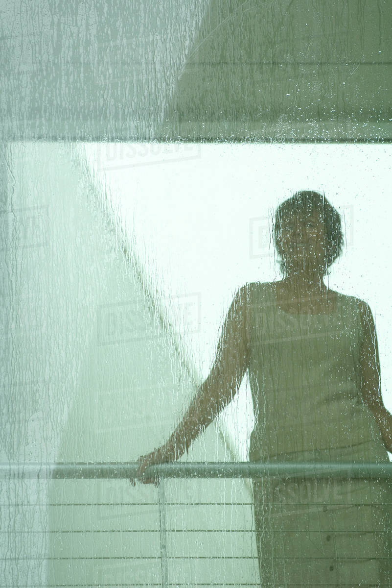 Silhouette of woman looking through window in rain - Stock Photo - Dissolve