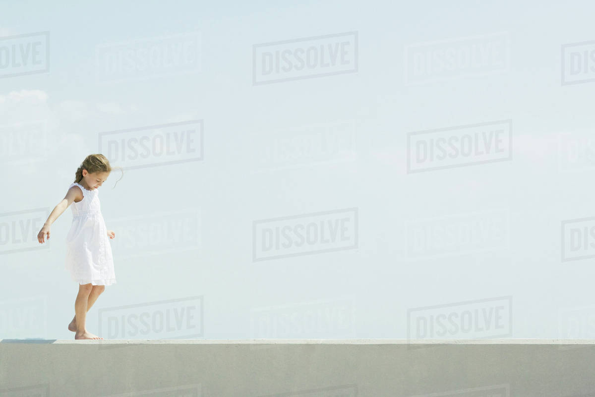 Little girl walking across low wall, arms out, looking down - Royalty ...