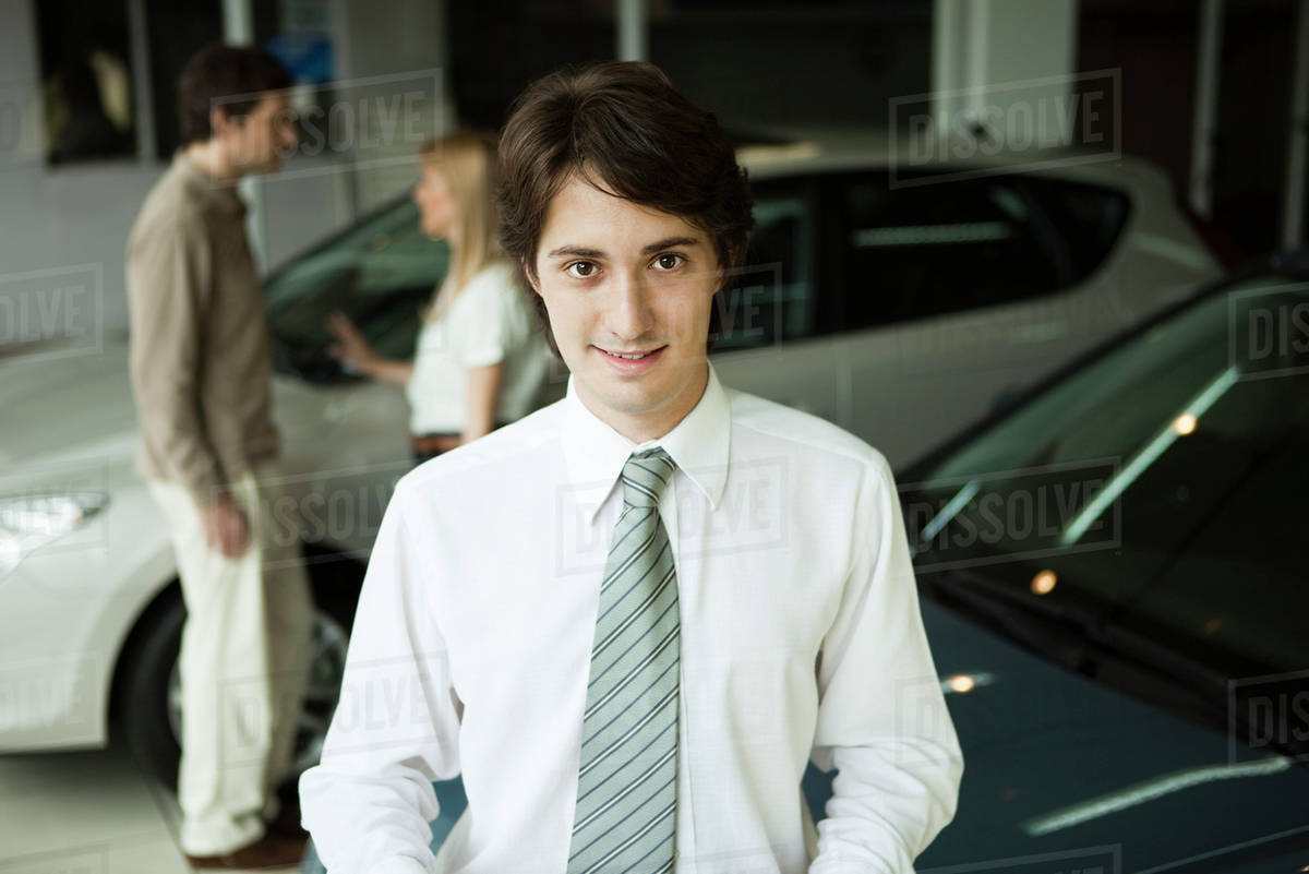 Car salesman in car dealership showroom, potential buyers in background ...