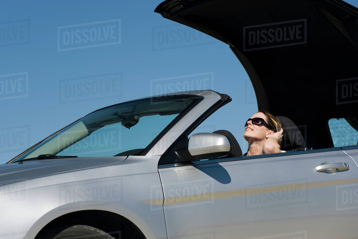 Woman putting convertible top down preparing for drive on summer day ...