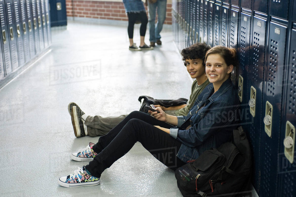 High school student sitting on floor with friend by lockers in school ...