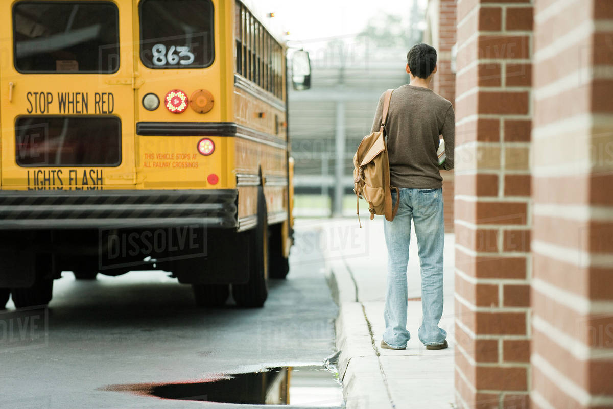 High school student waiting outside school for bus - Stock Photo - Dissolve