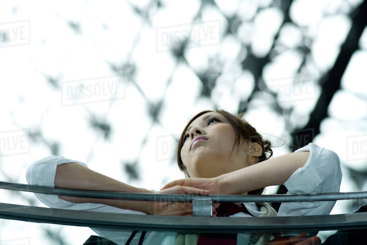 Young woman leaning against railing with arms folded, low angle view ...