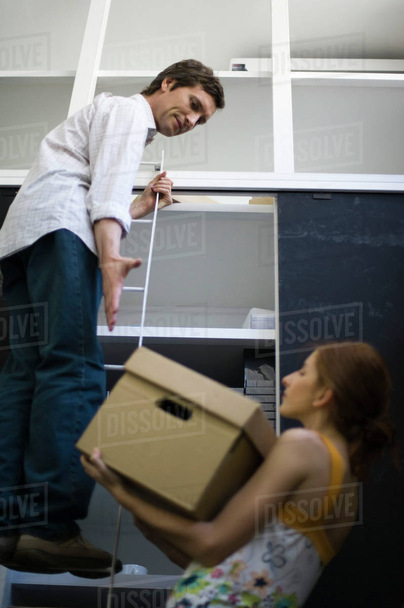 Woman struggling to lift heavy box up to man standing on ladder - Stock ...