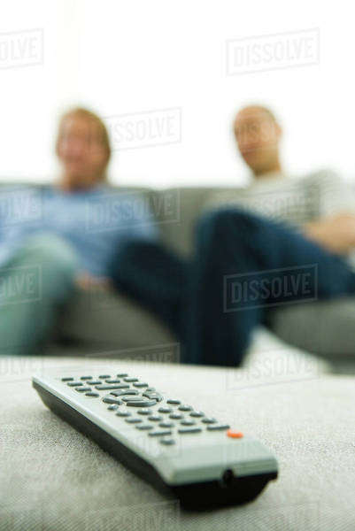 Close-up of remote control, men sitting on sofa in background - Stock ...