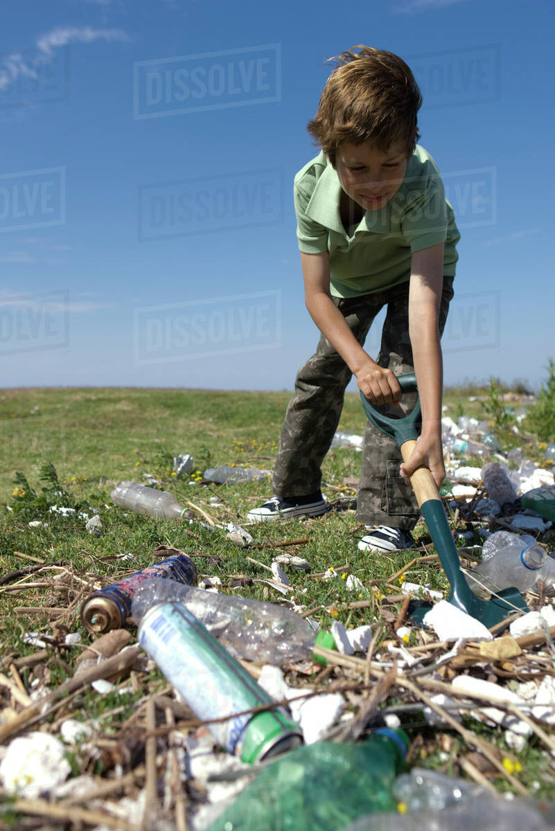 Boy shoveling trash in field - Royalty-free Stock Photo | Dissolve