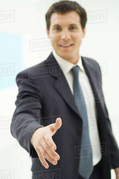 Businessman holding hand out toward camera, smiling, personal ...