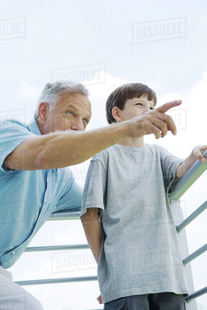 Grandfather and grandson standing by railing together, man pointing ...