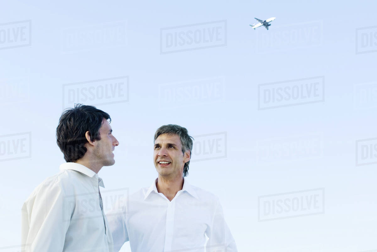 Two men talking to each other, airplane high in the background - Stock ...