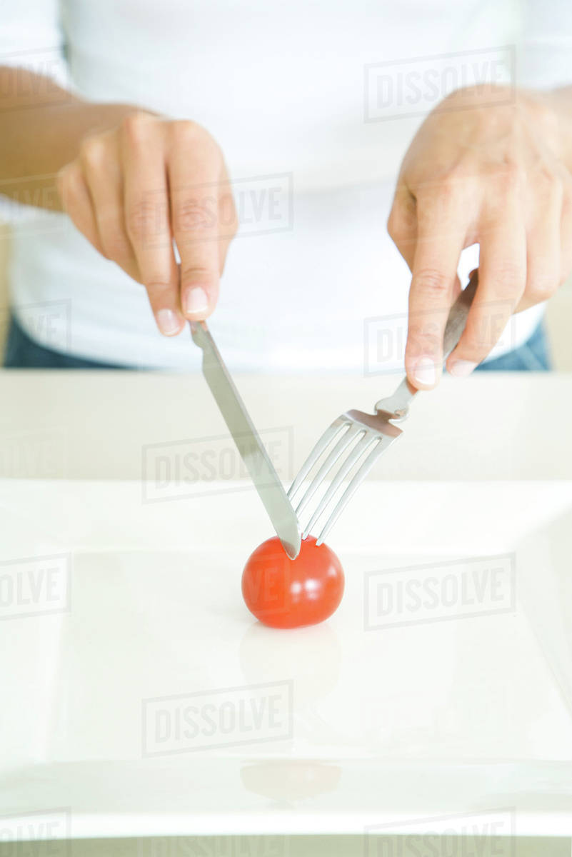 Woman cutting single cherry tomato with fork and knife, cropped view ...