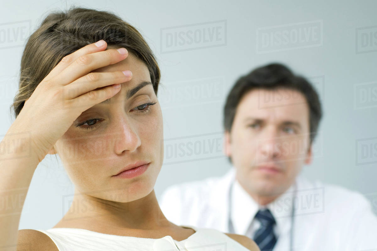 Woman holding head, looking down, doctor in background - Royalty-free ...
