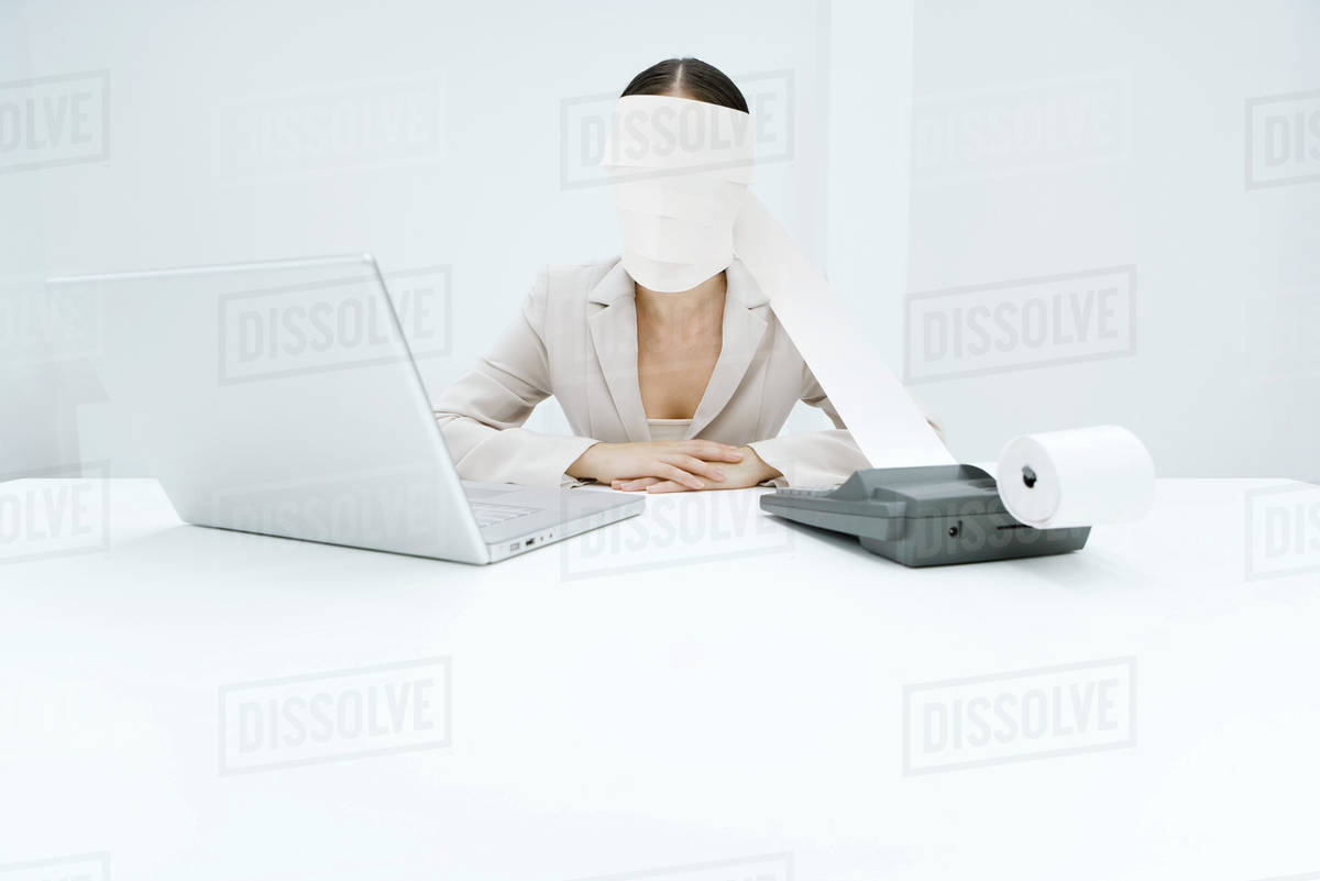Woman sitting at desk with adding machine and laptop, printout tape ...