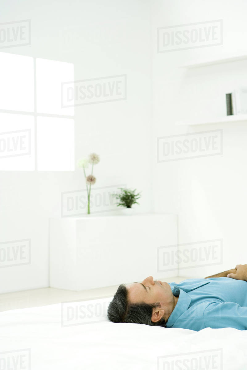 Man lying on back on bed, eyes closed - Stock Photo - Dissolve