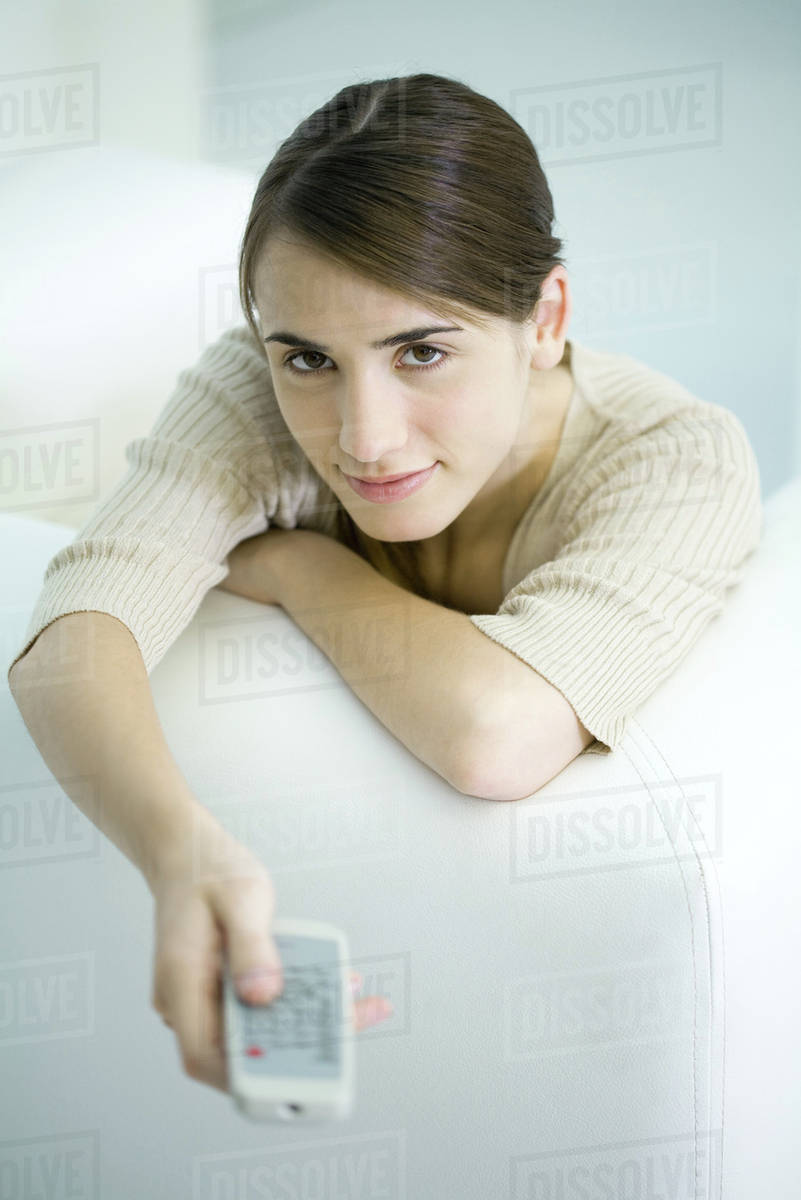 Woman leaning over side of couch, pointing remote control, smiling at ...