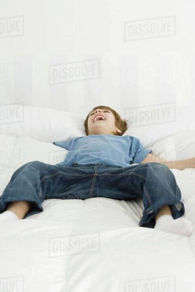 Boy lying on bed, laughing - Stock Photo - Dissolve