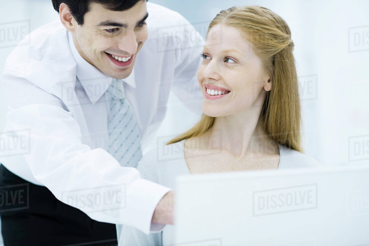 Professional man leaning over female colleague's shoulder, pointing at ...