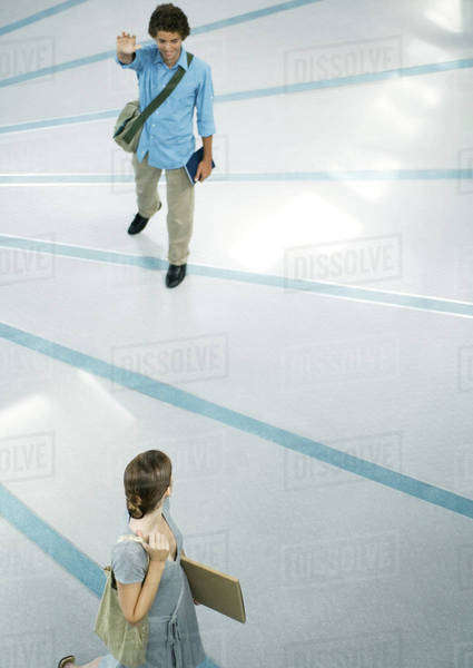 Teenage boy wearing messenger bag waving to female friend, full length ...