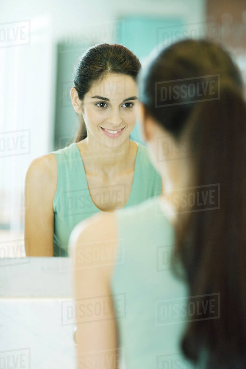 Young woman looking at self in mirror - Royalty-free Stock Photo | Dissolve