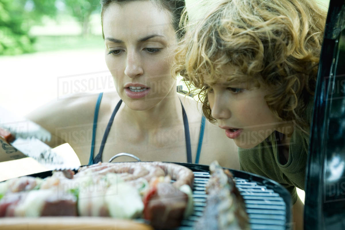 Family having cookout, woman and boy looking at meat grilling on ...