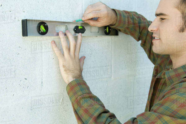 Man using level to draw line on wall - Stock Photo - Dissolve