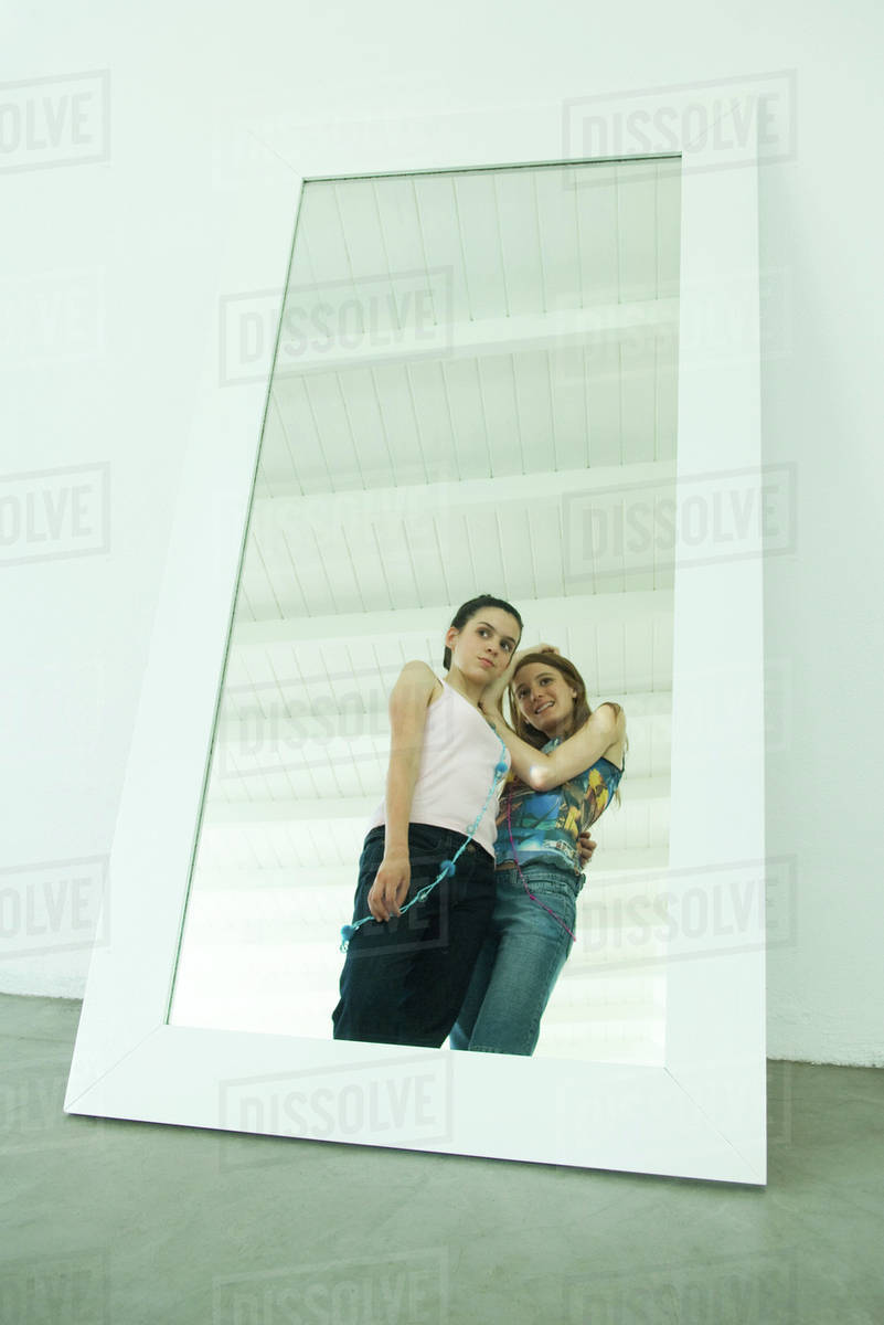 Two young friends standing together, looking at selves, reflected in ...