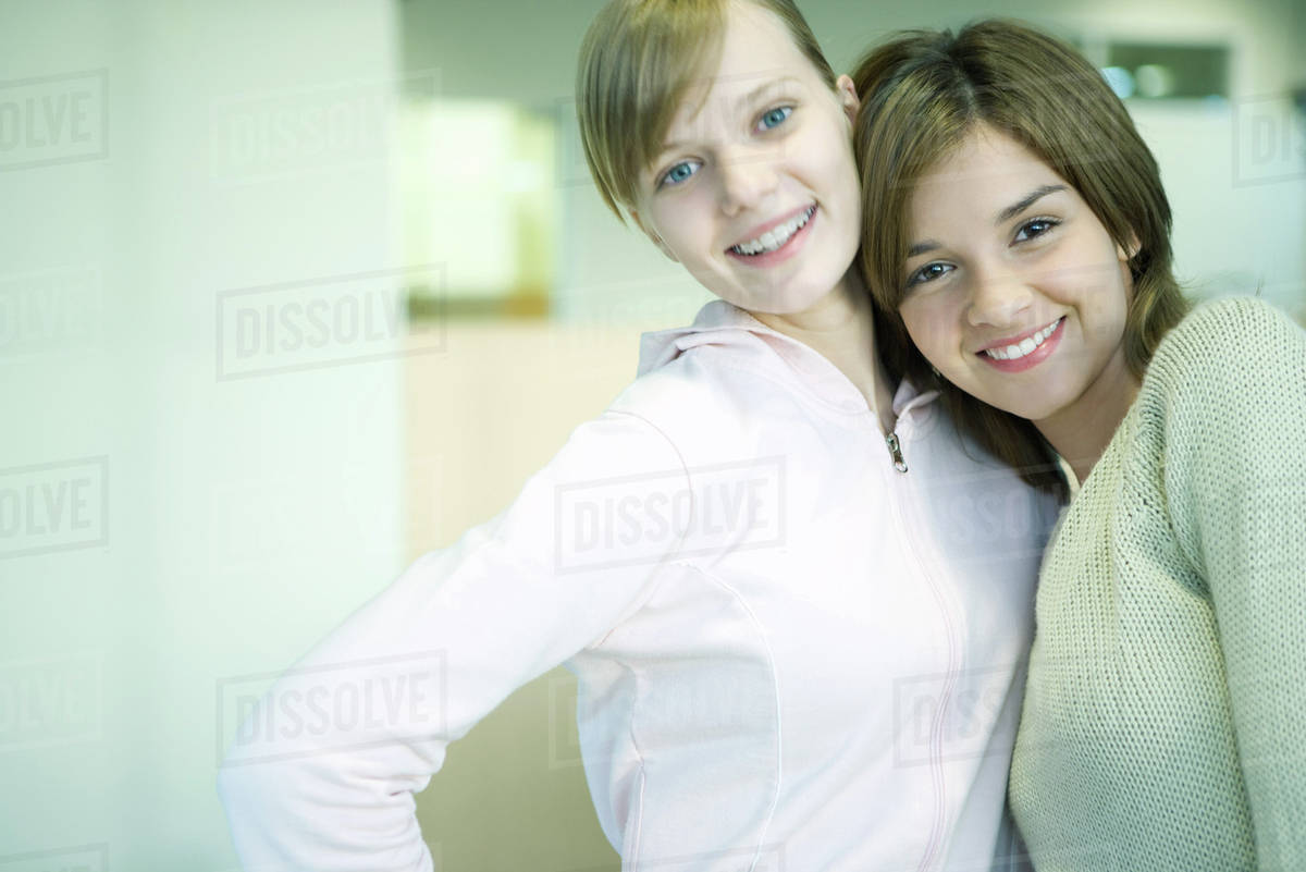 Two young friends standing together, smiling, one leaning her head on ...