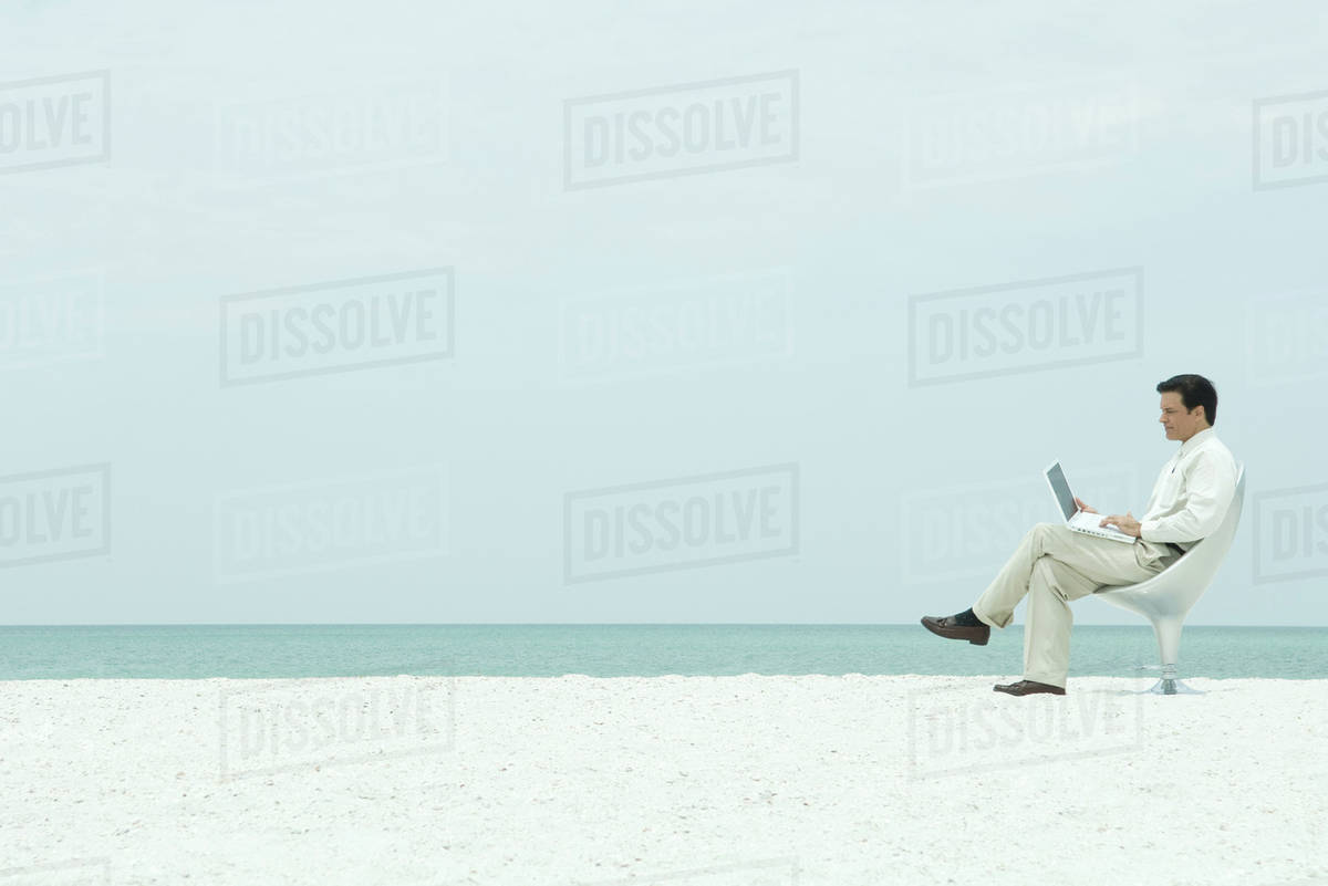 Businessman using laptop computer on the beach, full length - Stock ...