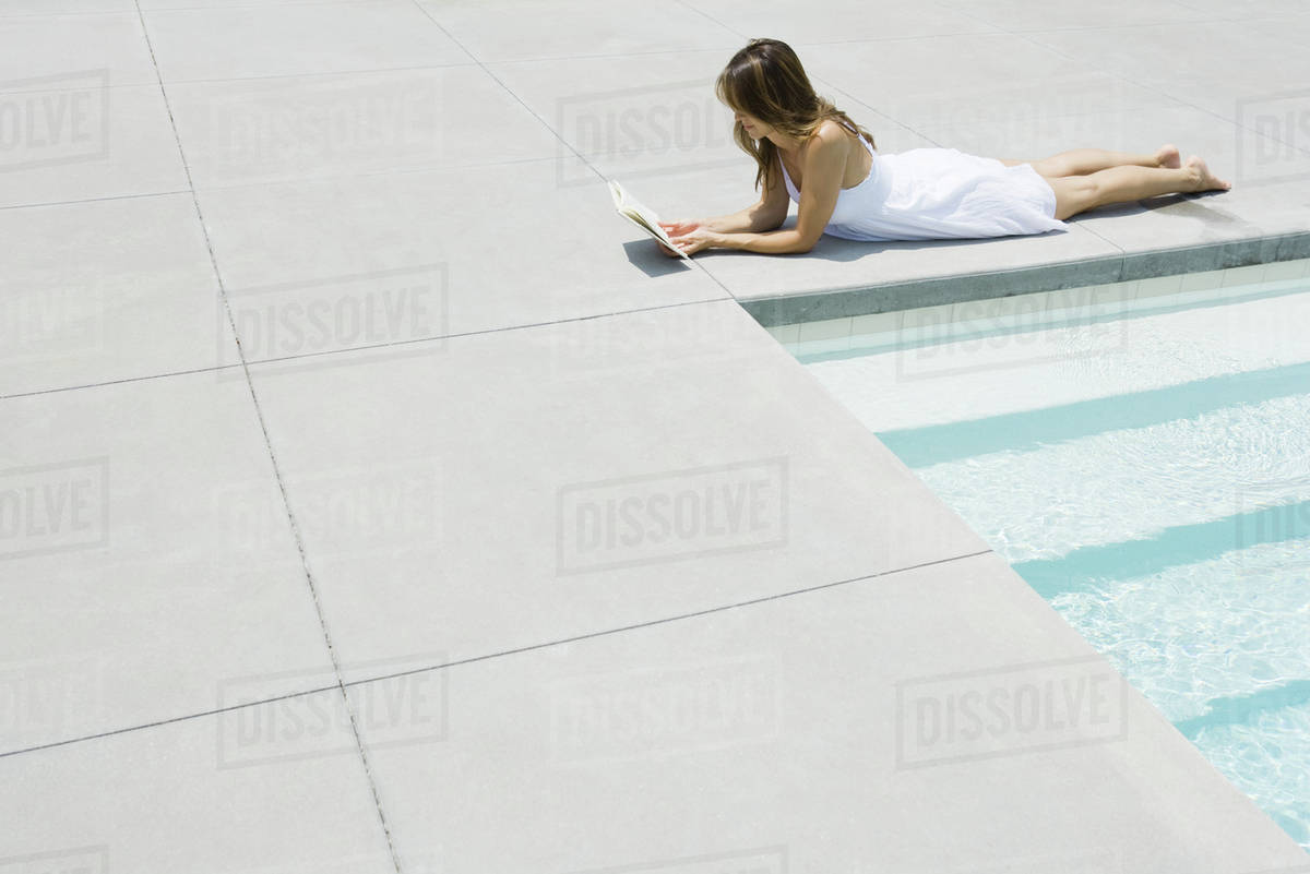 Woman in sundress lying by edge of pool, reading, full length - Stock ...