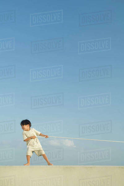 Little boy pulling on rope, blue sky in background, full length ...