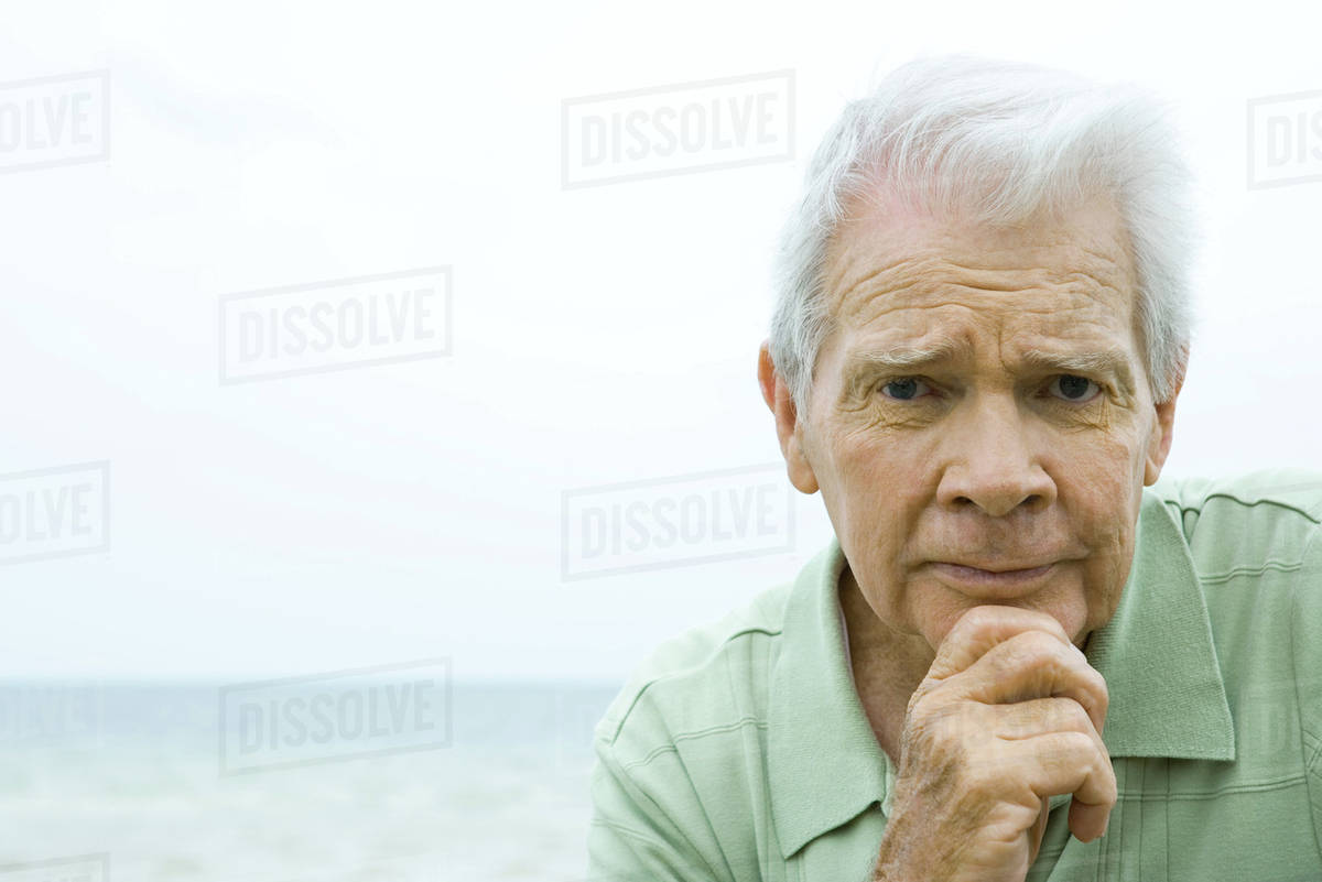 Senior man furrowing brow, hand under chin, looking at camera - Stock ...