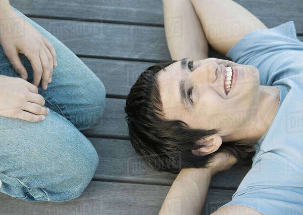 Young man reclining on the ground with hands behind head, smiling ...