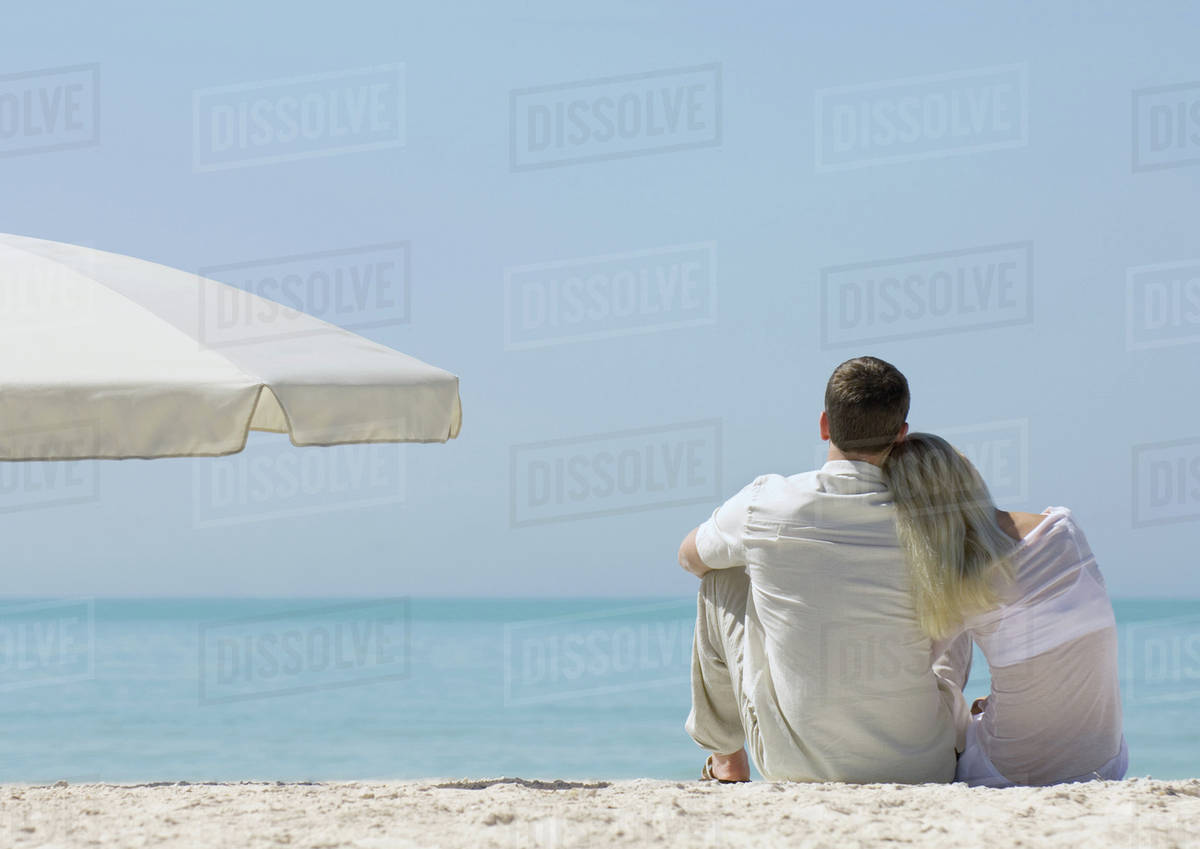 Couple sitting on beach, woman resting head on man's shoulder, rear ...