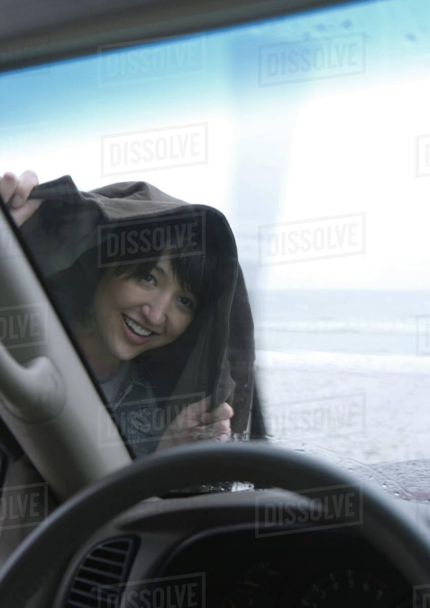 Woman holding jacket over head, looking through car windshield ...