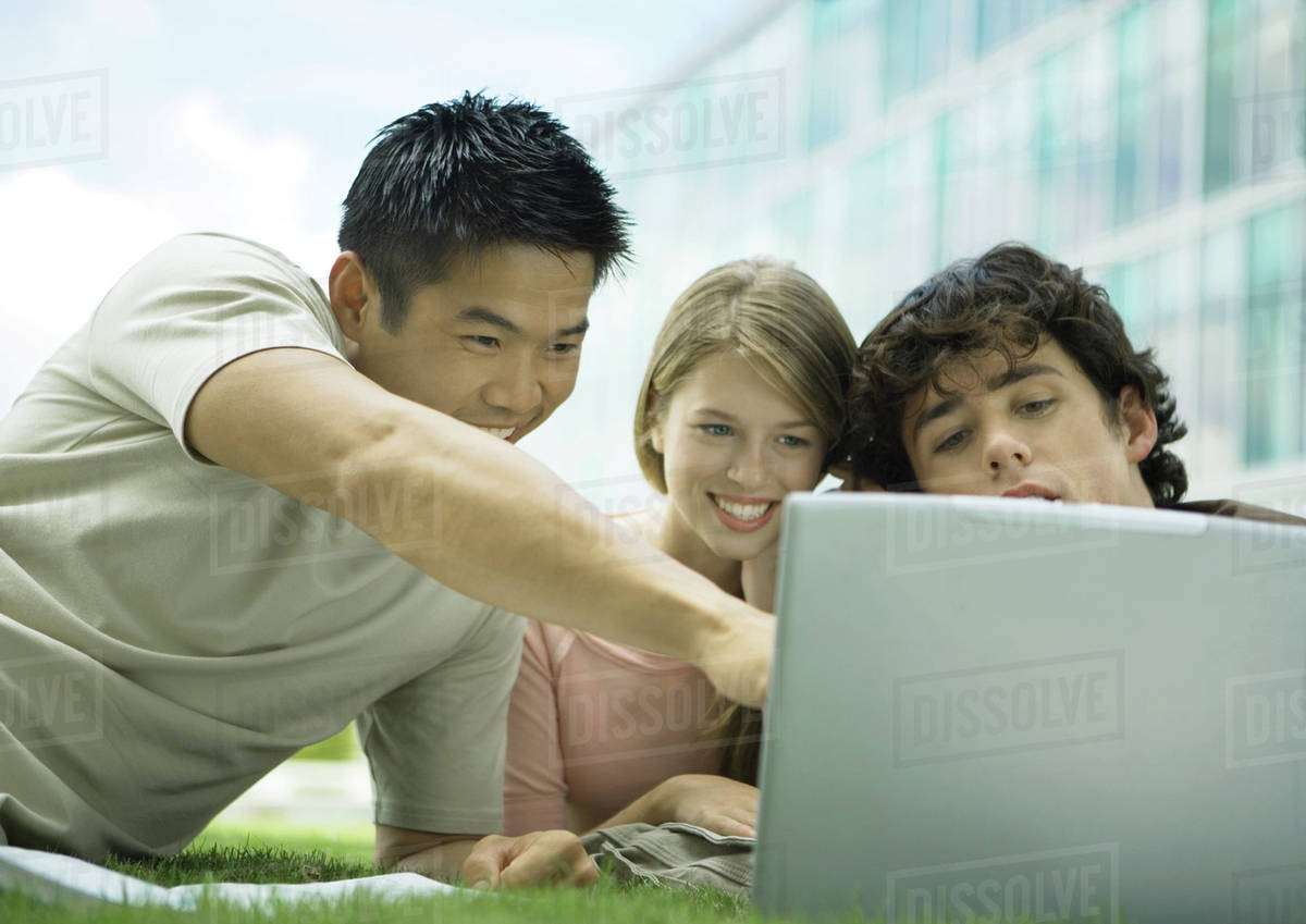 Three college students using laptop outdoors - Stock Photo - Dissolve