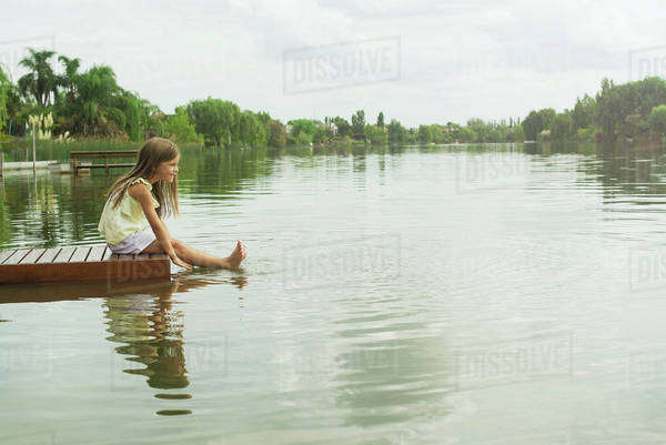 Girl sitting on dock with feet dangling in lake, portrait - Royalty ...