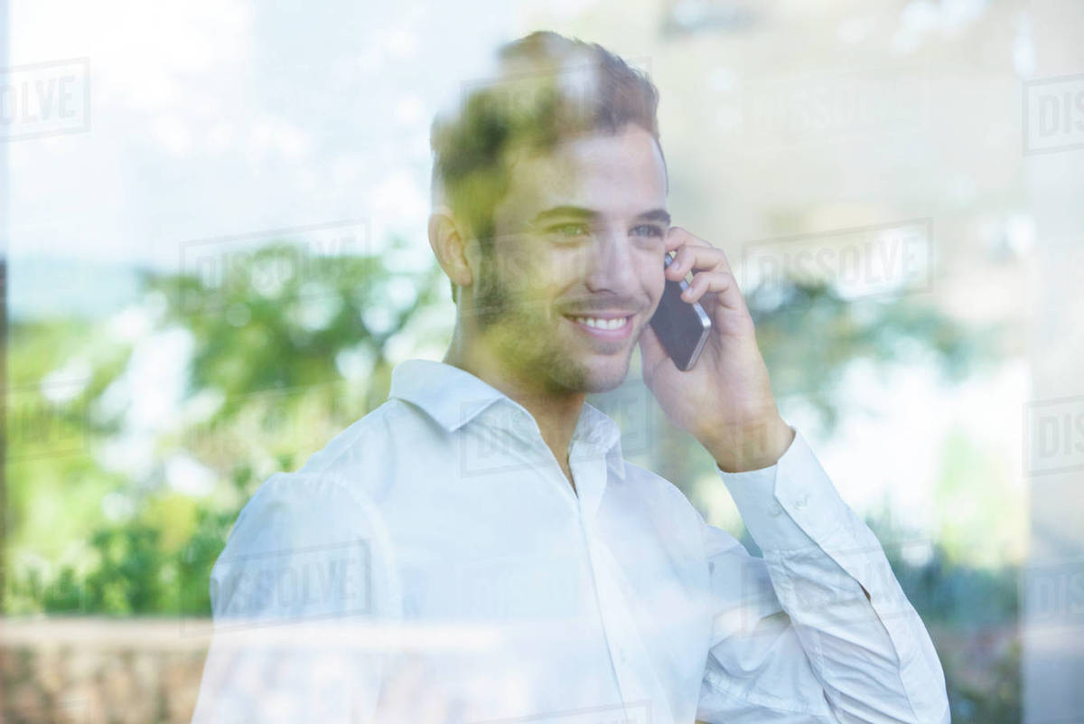 Businessman looking out of window from office while using cell phone ...