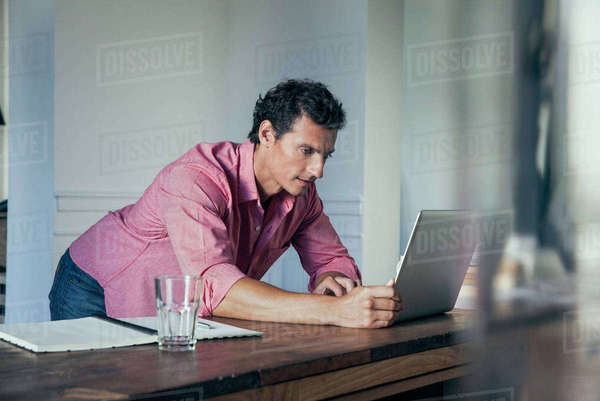 Man leaning against table, using laptop computer - Stock Photo - Dissolve