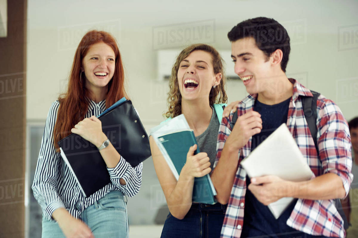 Classmates laughing together while walking in school corridor - Stock ...