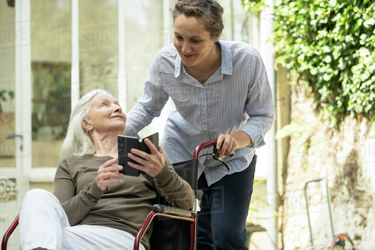 Senior female patient showing mobile phone to young home carer ...