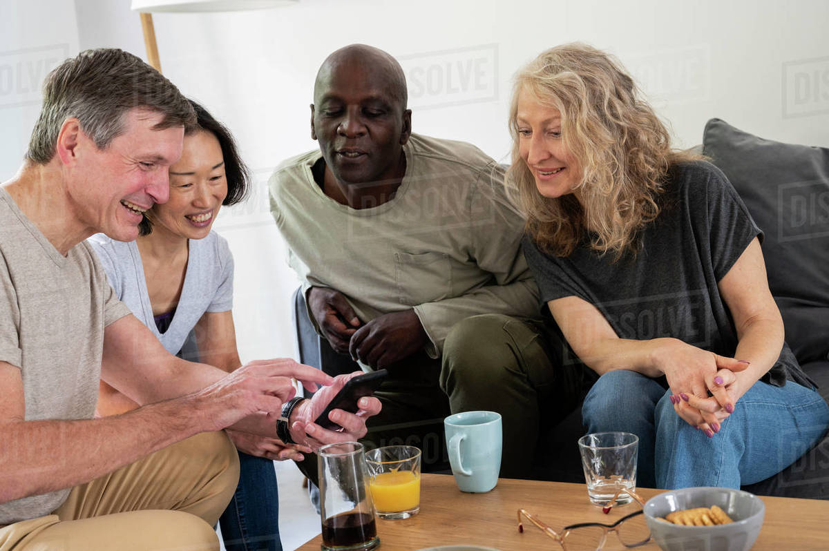 Fun diverse group of middle-aged friends looking at photos on cell ...