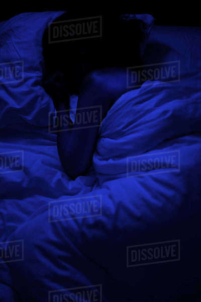 Person sleeping in bed in darkness - Stock Photo - Dissolve