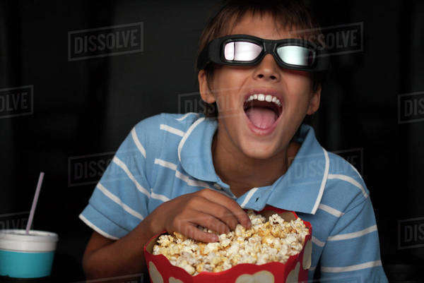 Boy laughing and eating popcorn during 3-D movie in theater - Stock ...