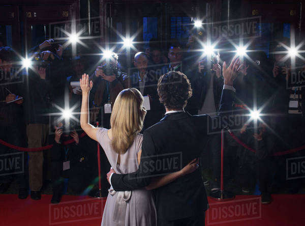 Rear view of celebrity couple waving to paparazzi at red carpet event ...