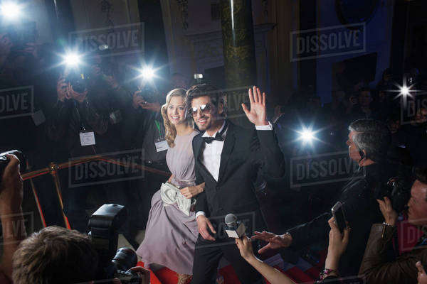 Well dressed celebrity couple waving to paparazzi on red carpet ...