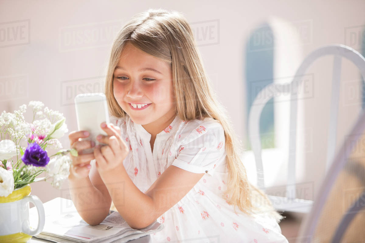 Girl using cell phone at table - Royalty-free Stock Photo | Dissolve