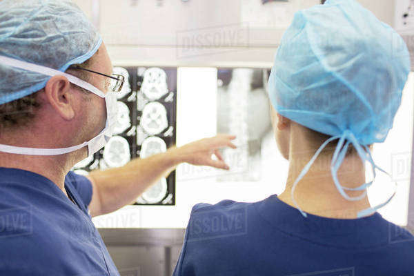 Rear view of surgeons looking at patient's x-ray and MRI scan in ...
