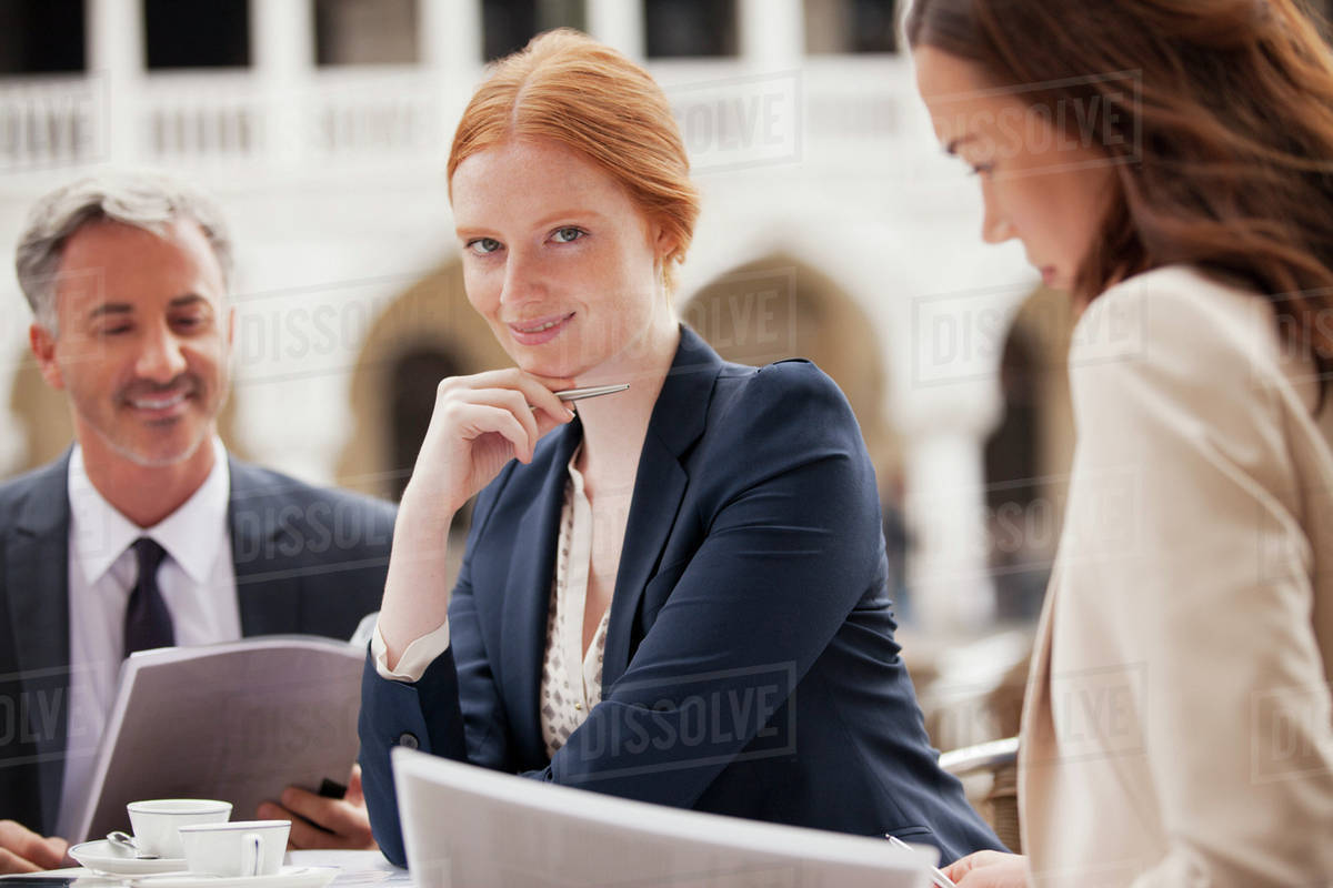 Portrait of smiling businesswomen working with co-workers at sidewalk ...