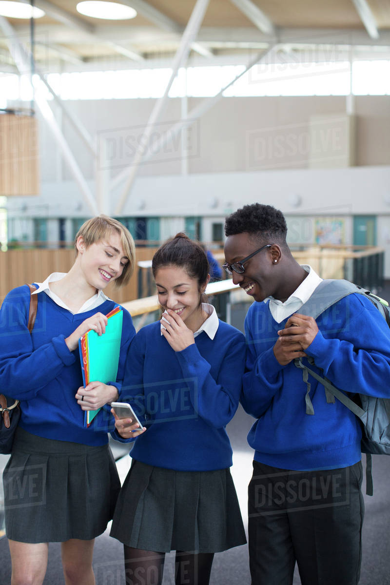 Three happy students wearing school uniforms using smartphone in school ...